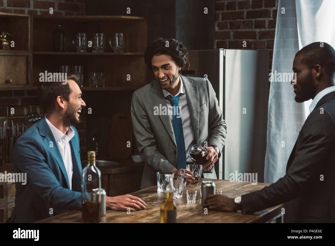 cheerful young male friends drinking alcohol beverages and talking ...