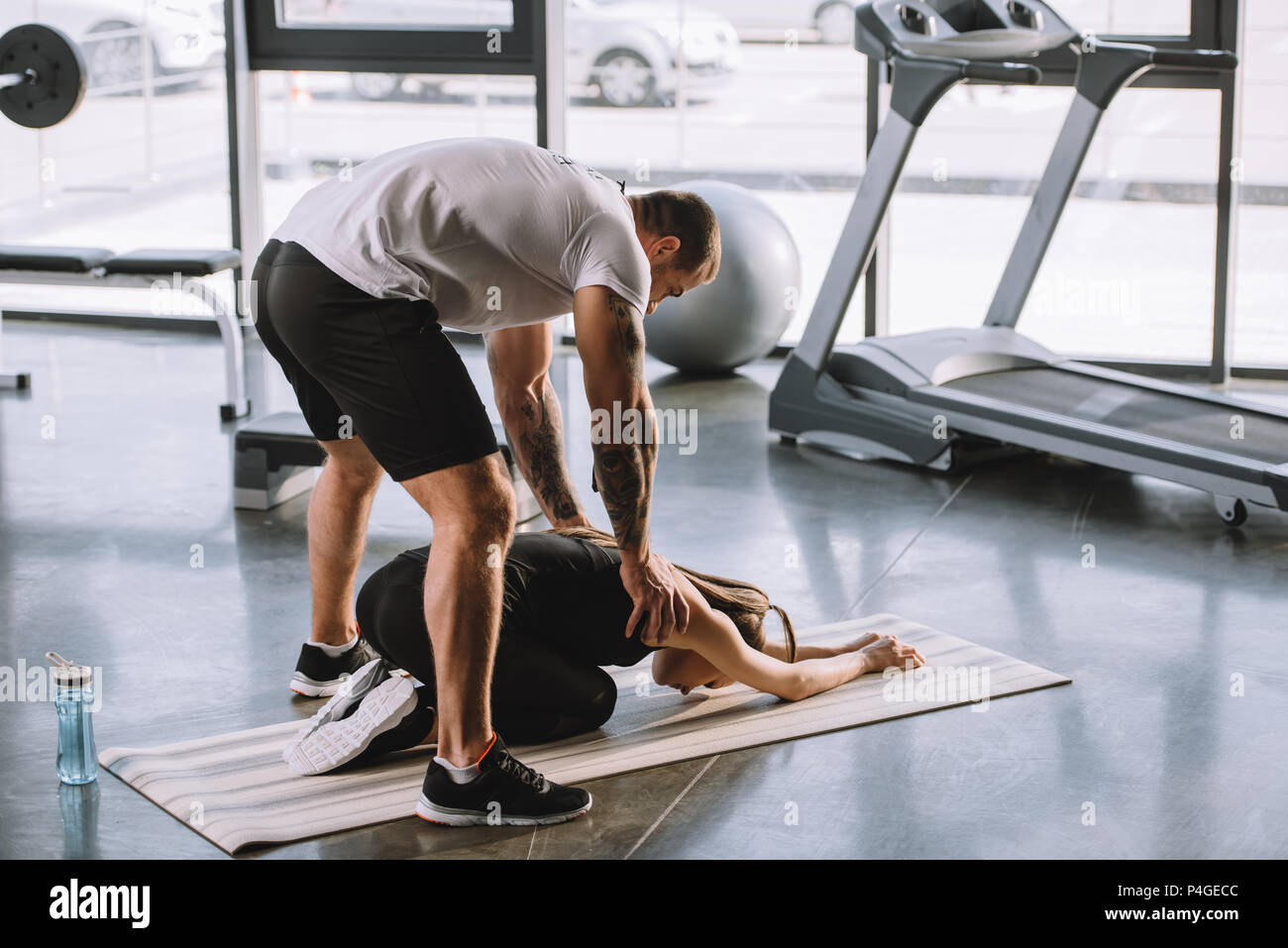 male personal trainer helping young athletic woman to stretching on ...