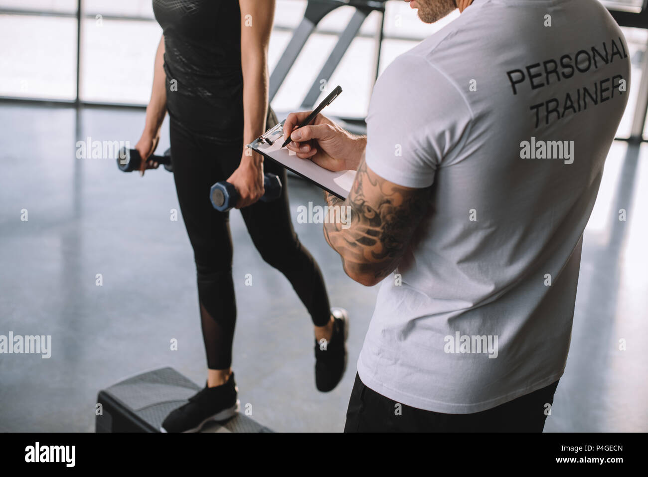 cropped image of male personal trainer writing in clipboard and young ...