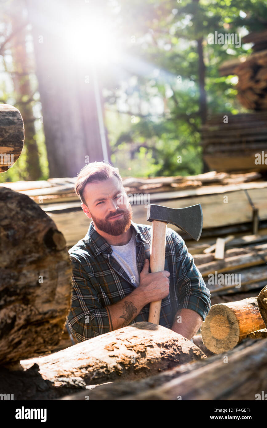 lumberjack in checkered shirt with tattooed hand holding axe at sawmill ...