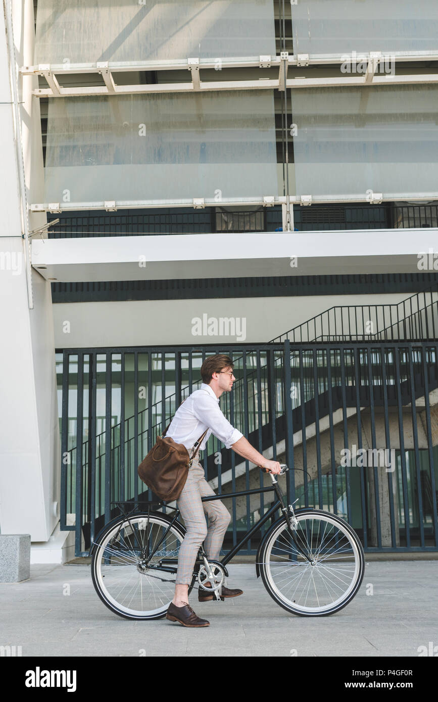 side view of stylish young man riding vintage bicycle on city street ...
