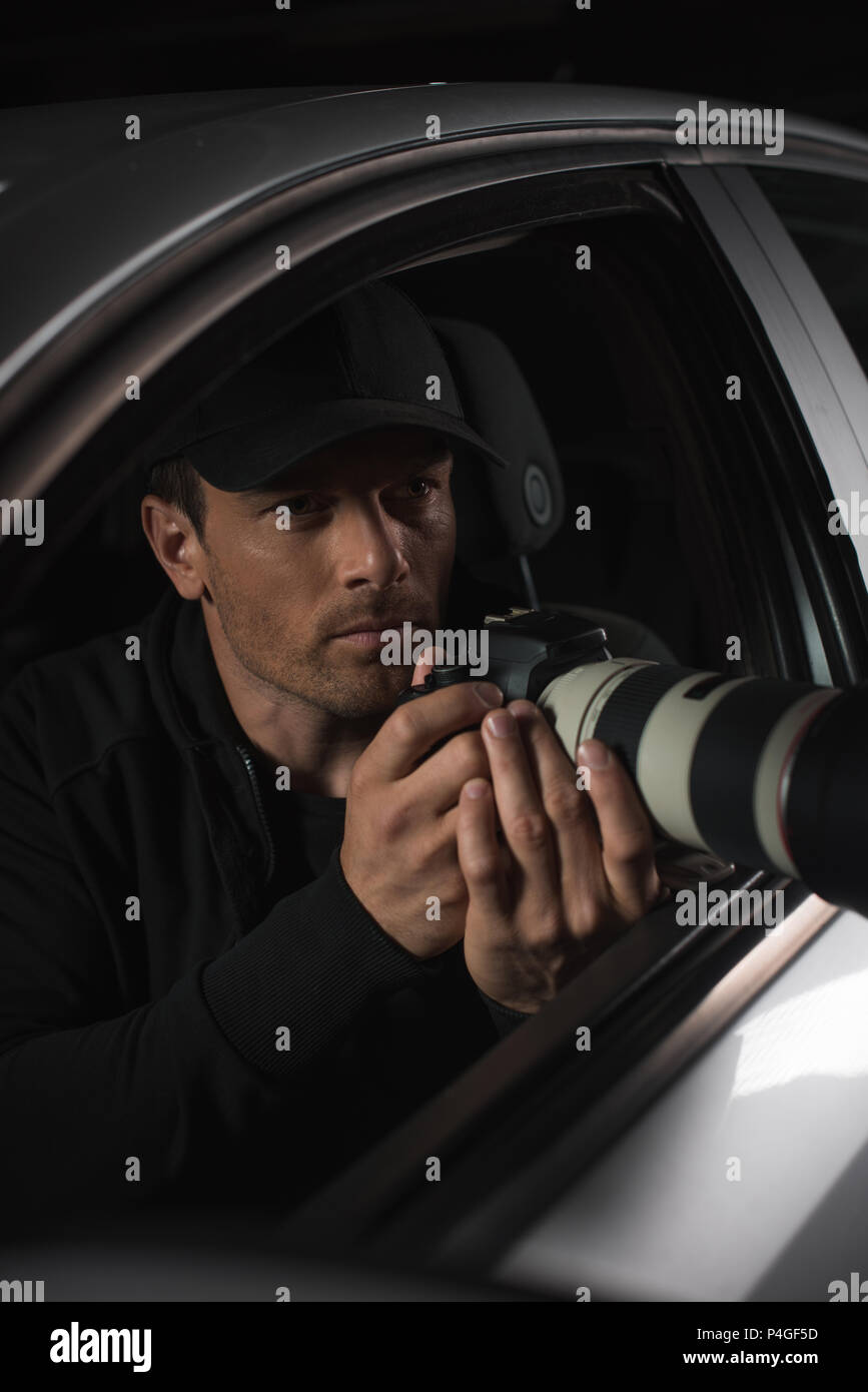 male paparazzi in cap doing surveillance by camera with object glass ...