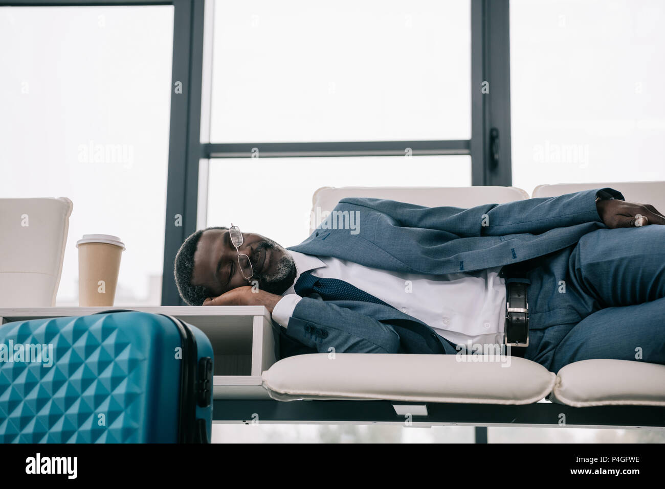 Middle aged African american businessman napping on chairs at airport ...