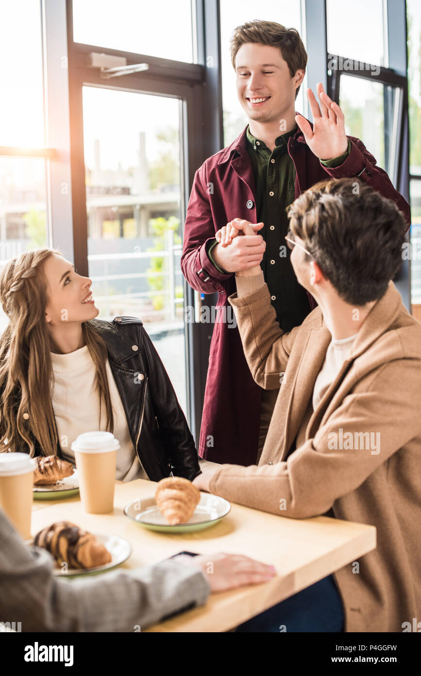 Man shaking hand to friend and waving hand to girls Stock Photo - Alamy