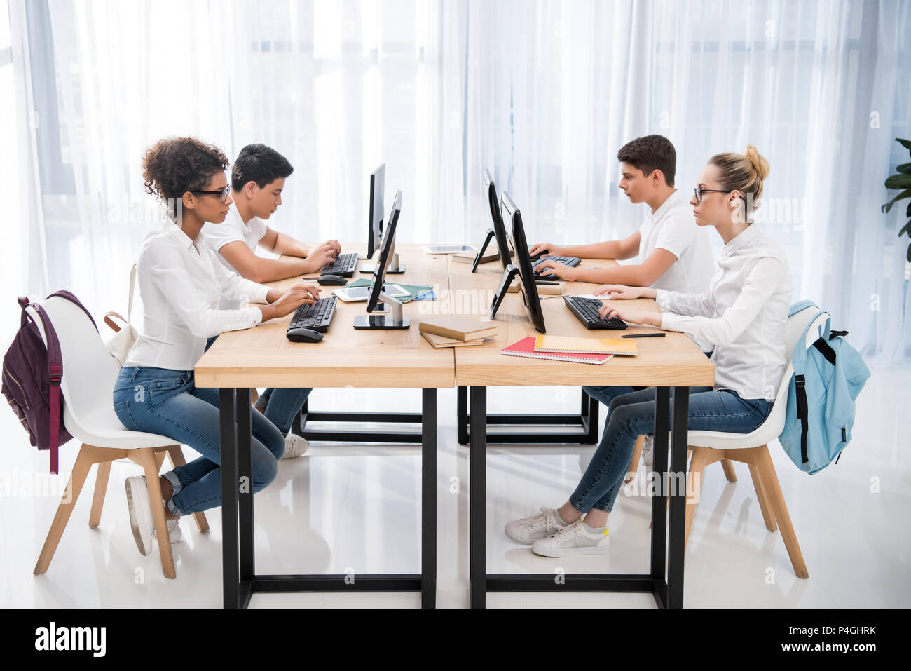 side view of four young multicultural students studying on computers ...