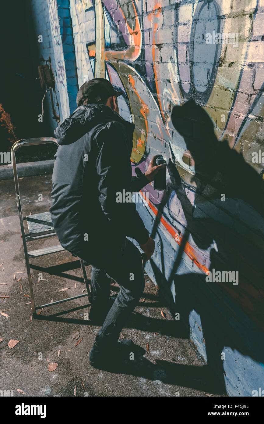man painting colorful graffiti on wall of building at night Stock Photo ...