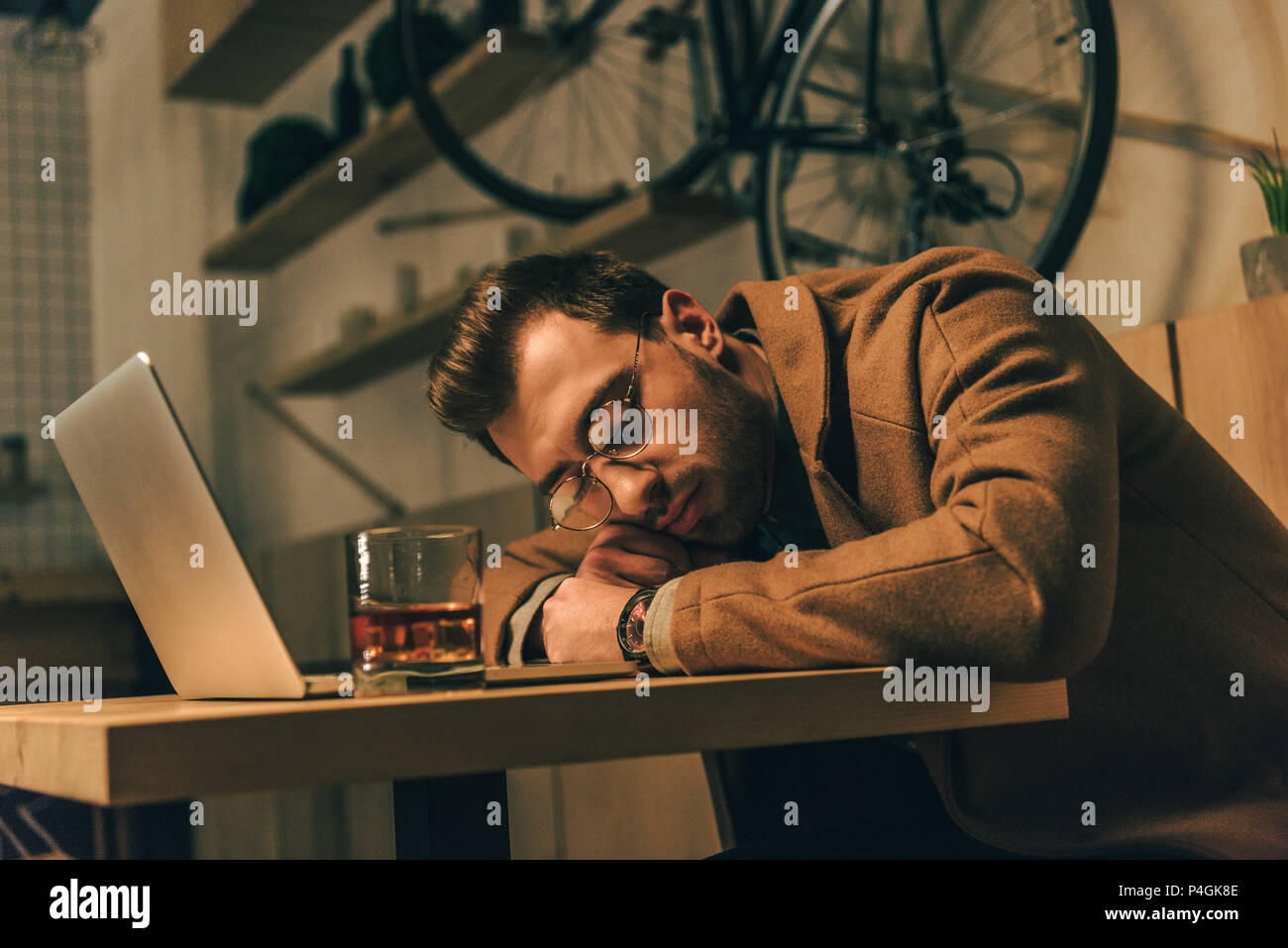 tired man sleeping on table with glass of whiskey and laptop in cafe ...