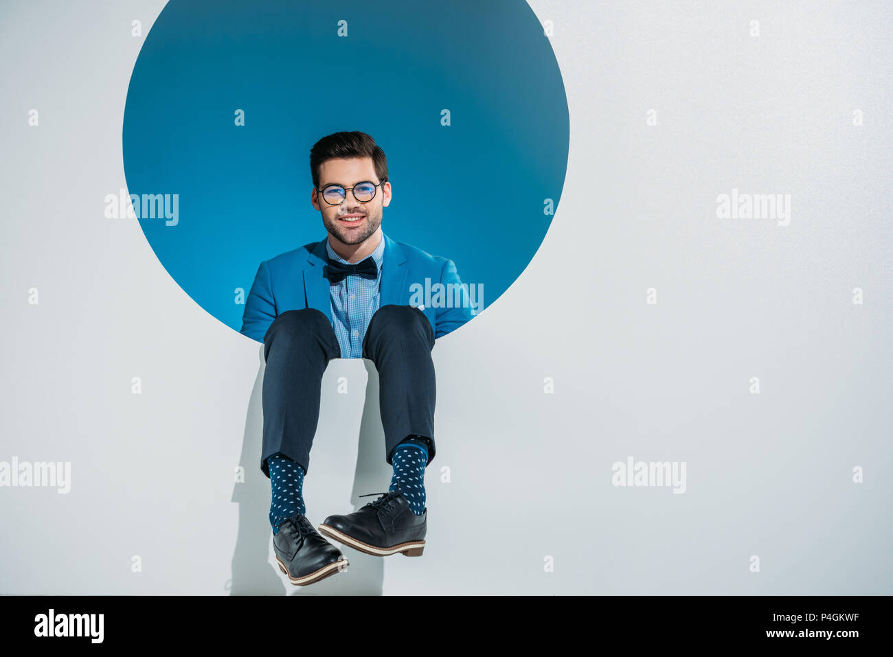 stylish young man smiling at camera while falling into hole on grey ...