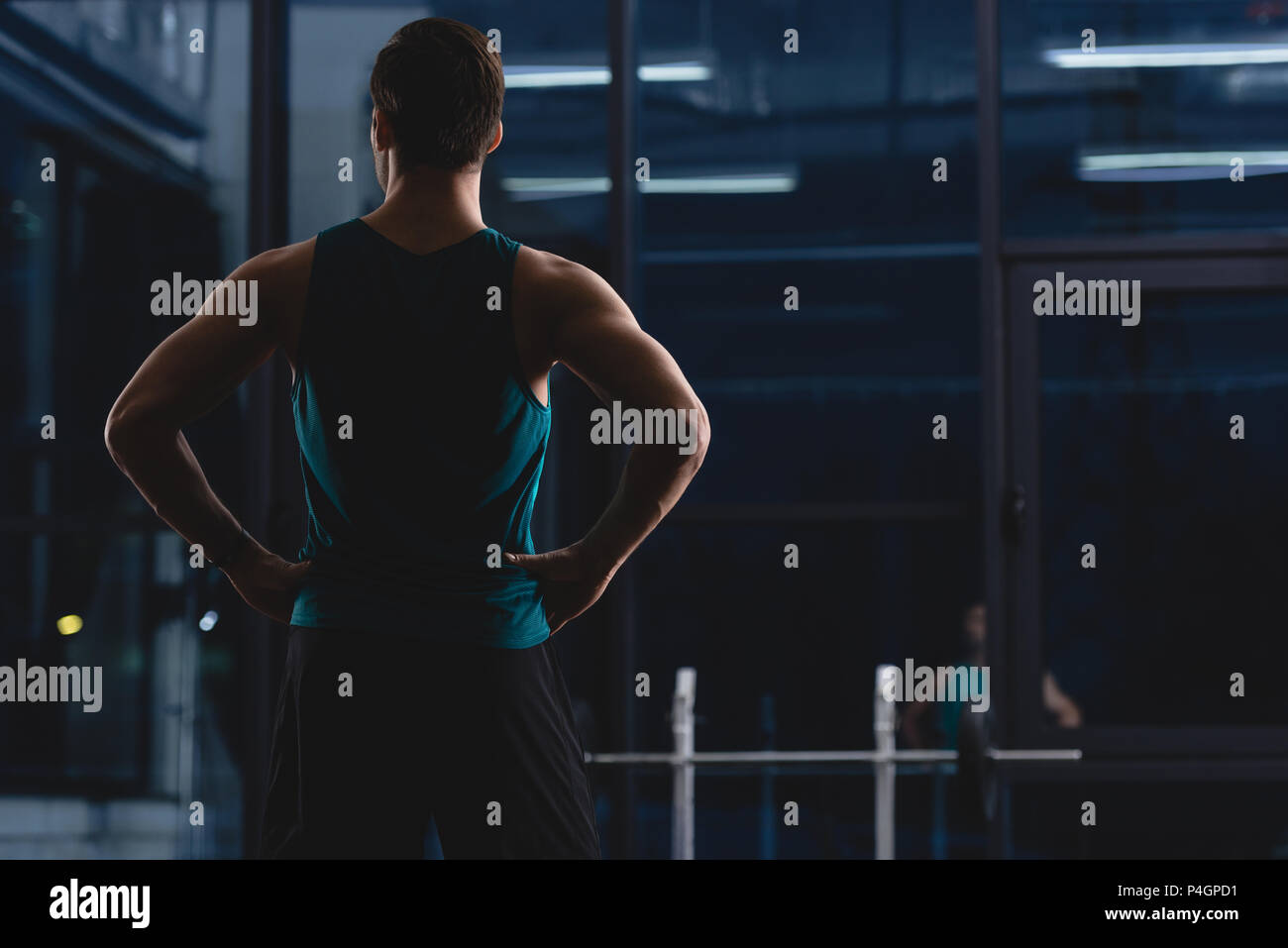 back view of silhouette of muscular sportsman standing in sports center ...