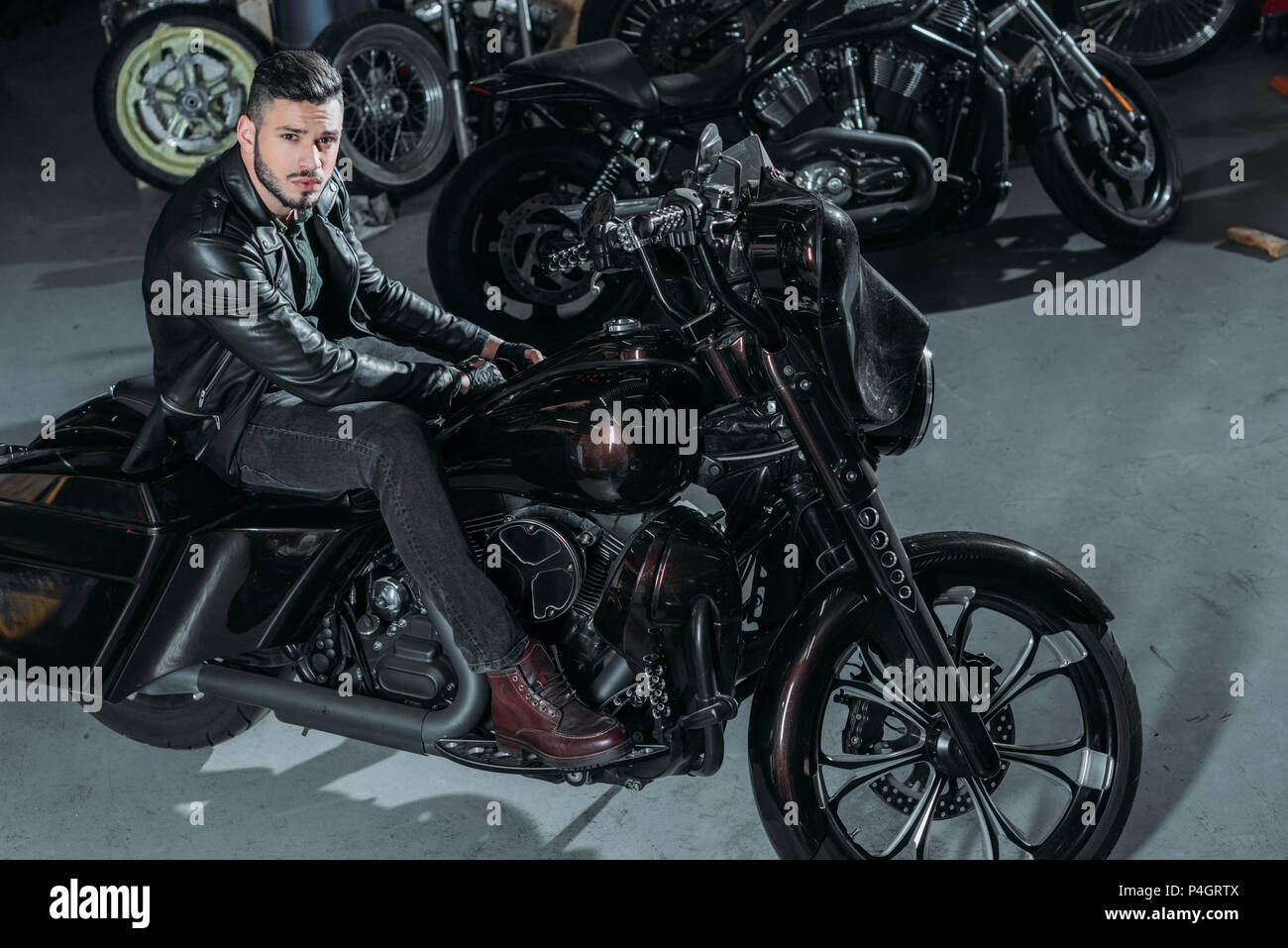 high angle view of handsome young man in leather jacket sitting on bike ...