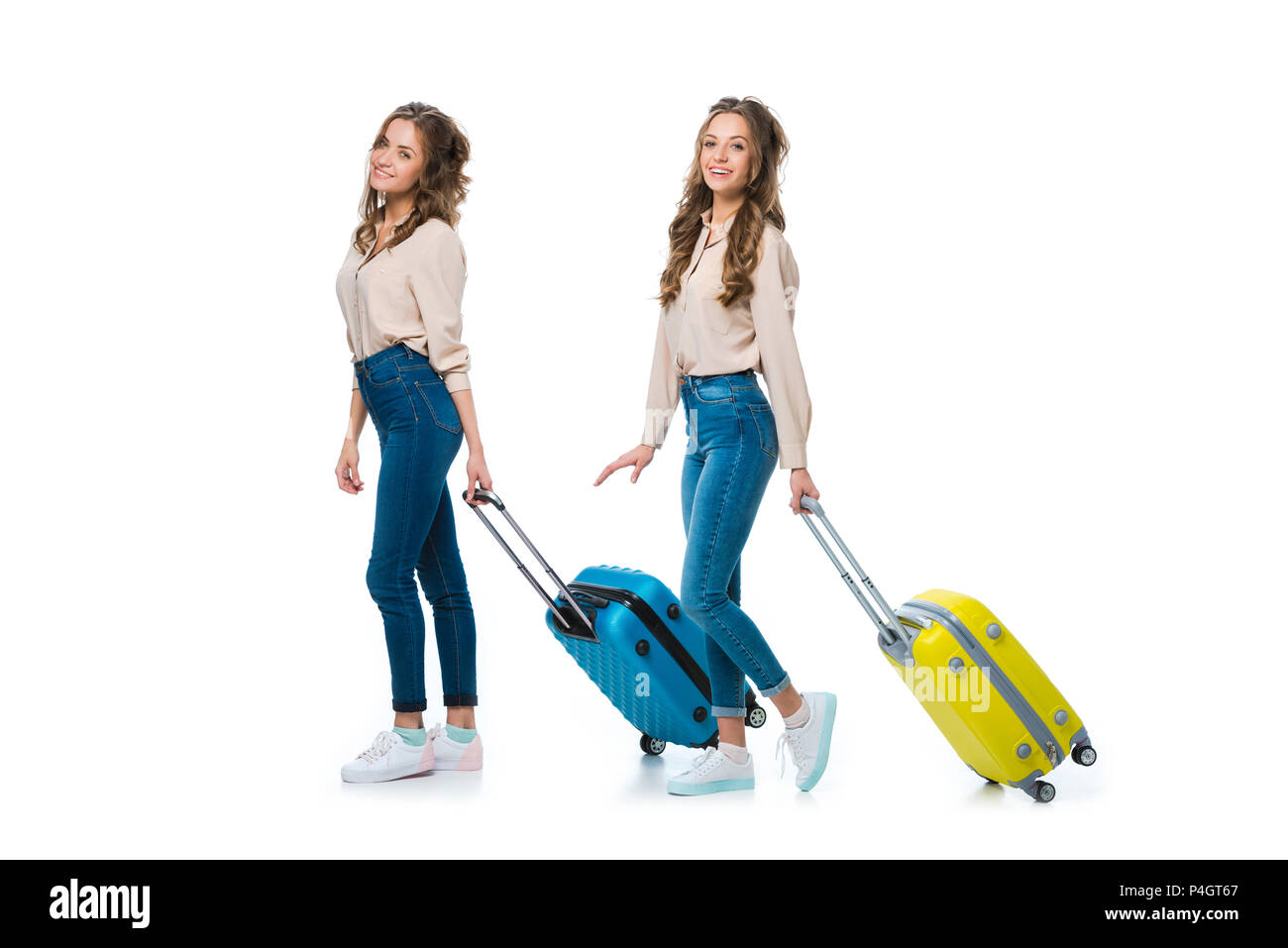side view of happy young twins with wheeled bags isolated on white ...