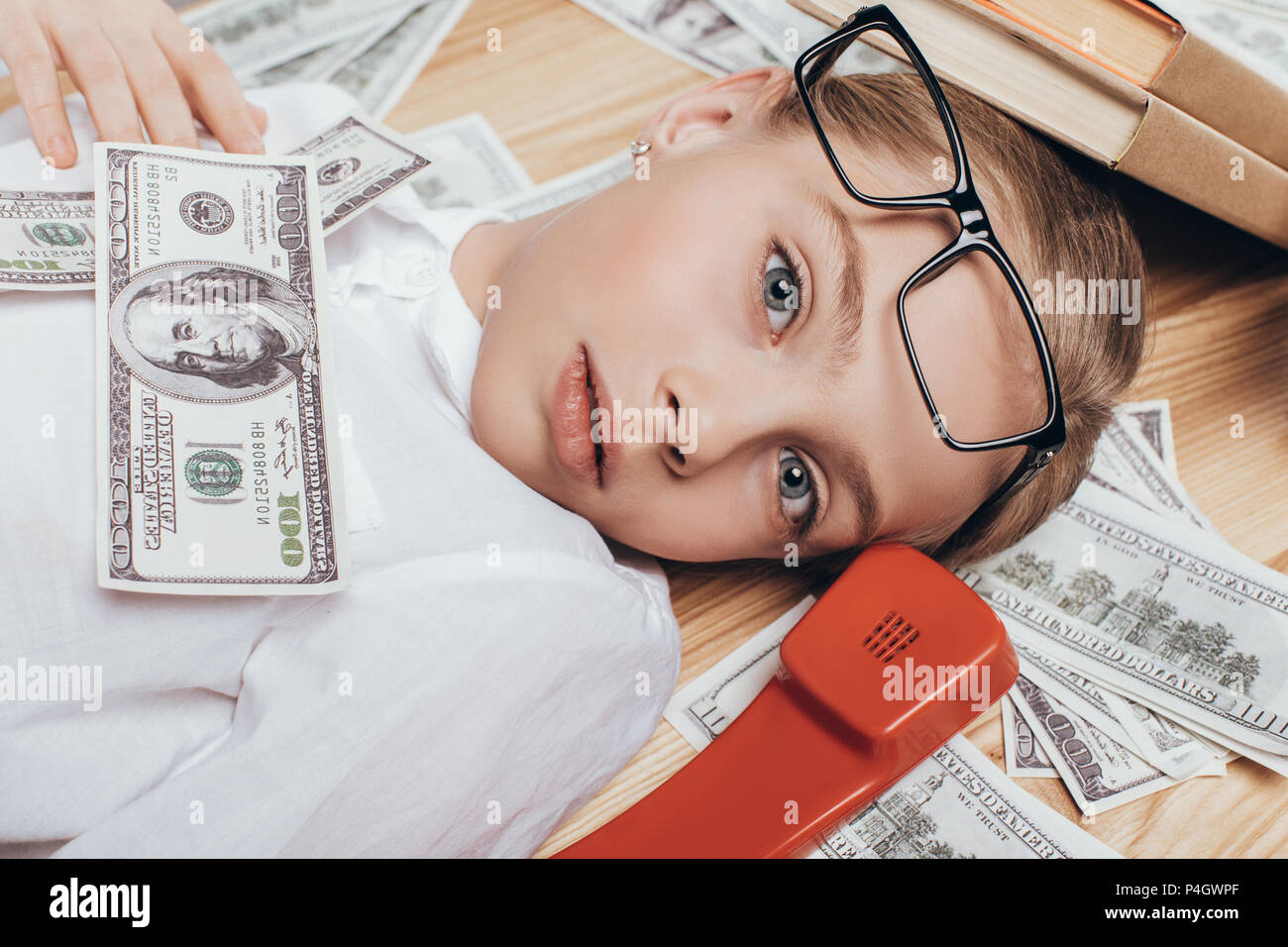 portrait of shocked little girl lying on table with money and telephone ...