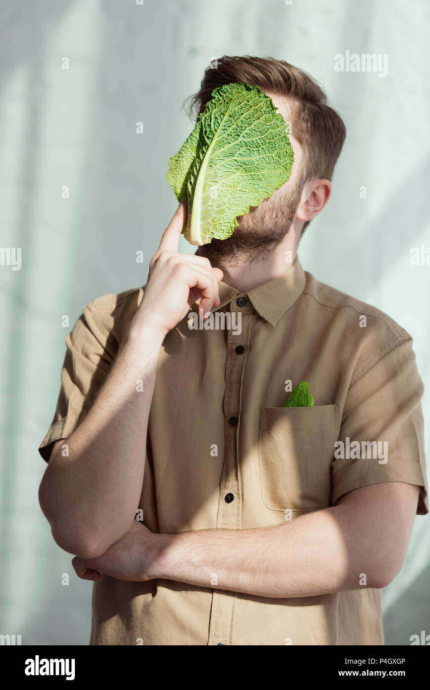 obscured view of pensive man with savoy cabbage leaf on face, vegan ...