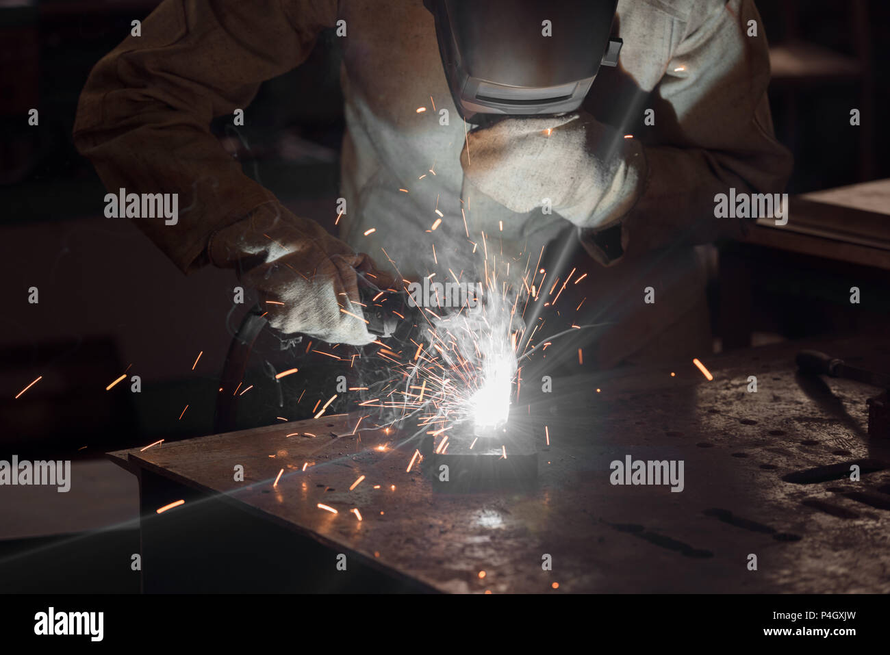 front view of welder in protection mask working with metal at factory ...