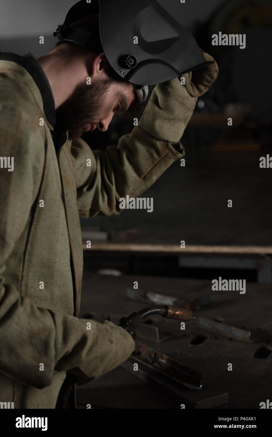 side view of welder lifting up protective mask to look at his work ...