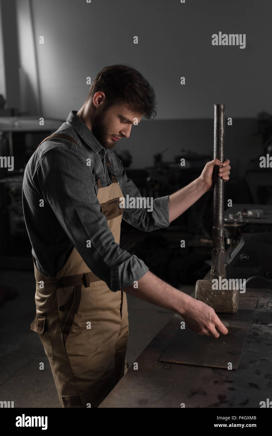 side view of young male worker hammering metal part at factory Stock ...
