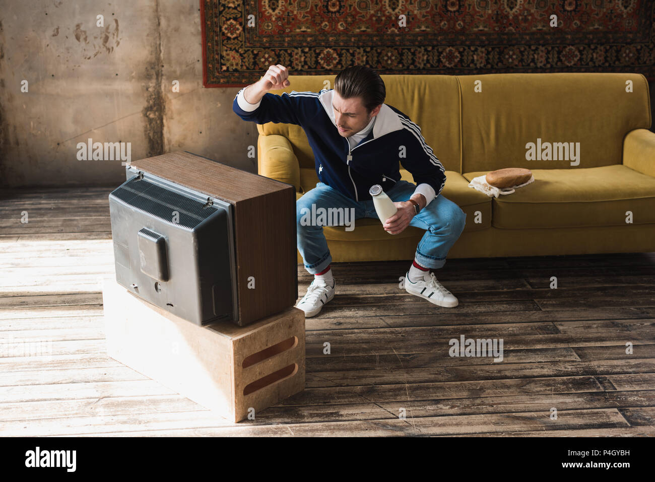 young man in vintage clothes with bottle of milk punching old tv Stock ...
