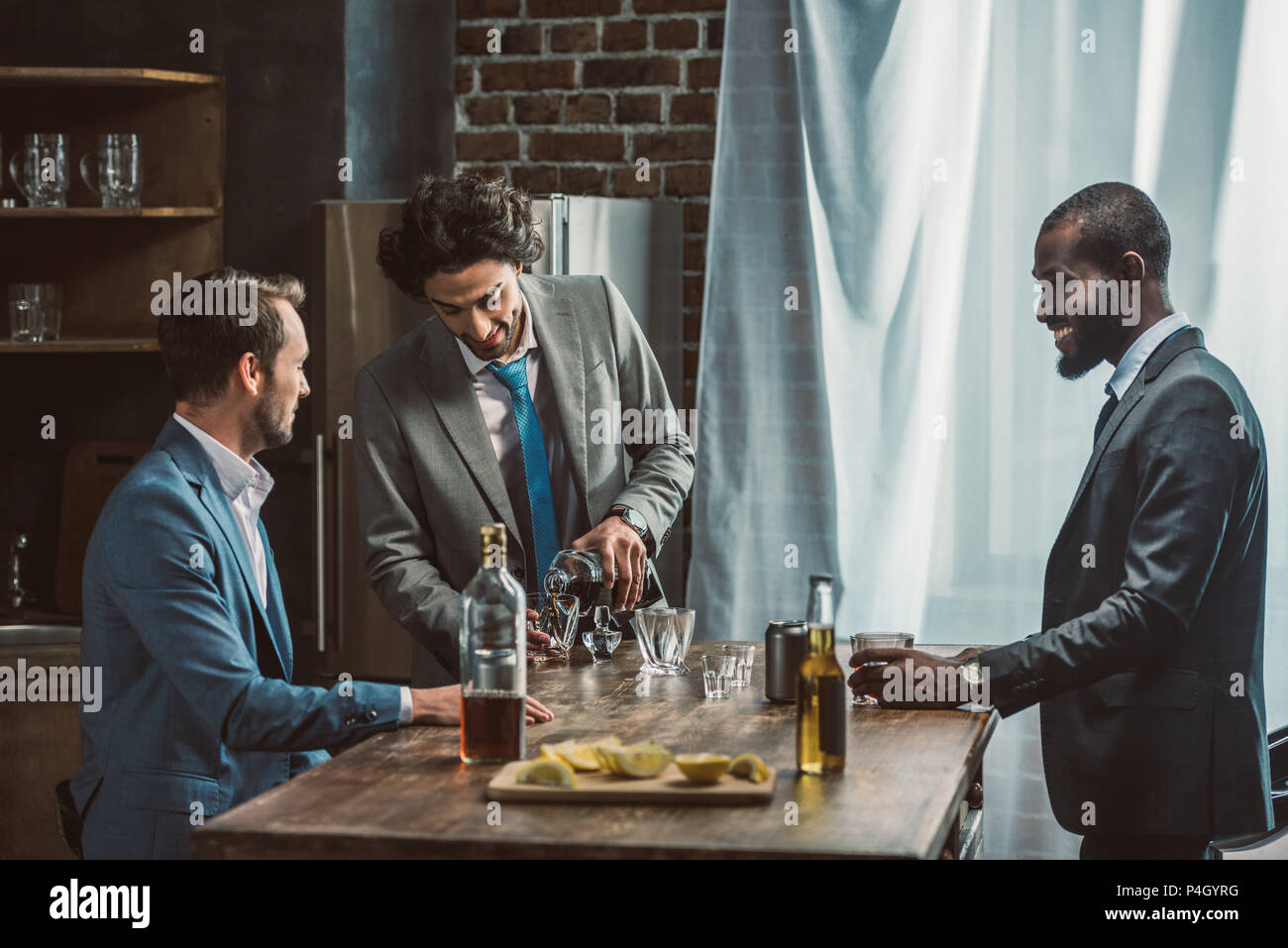 three smiling young multiethnic men in suits drinking alcohol beverages ...