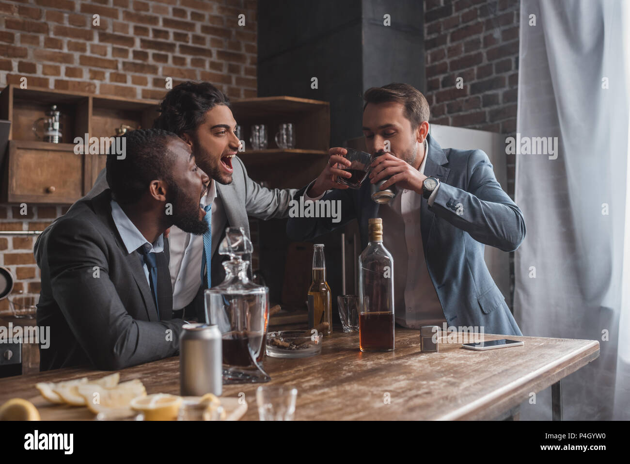 cheerful multiethnic men looking at friend drinking alcoholic beverages ...