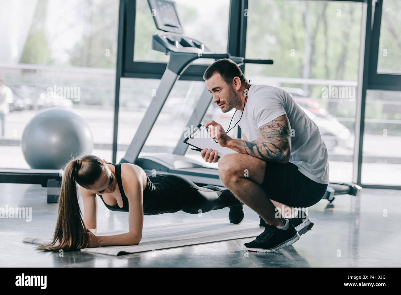 male personal trainer showing timer to young athletic woman doing plank ...