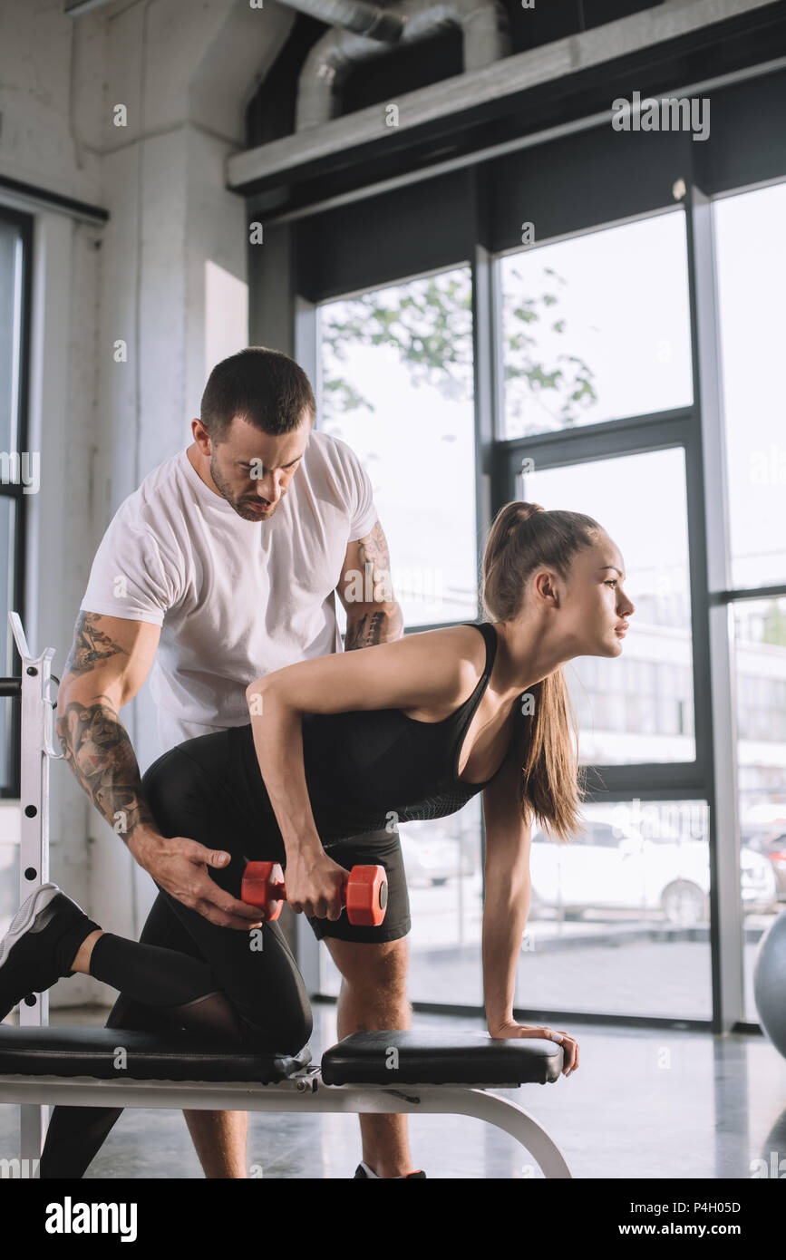 male personal trainer helping sportswoman to do exercises with dumbbell at gym Stock Photo - Alamy