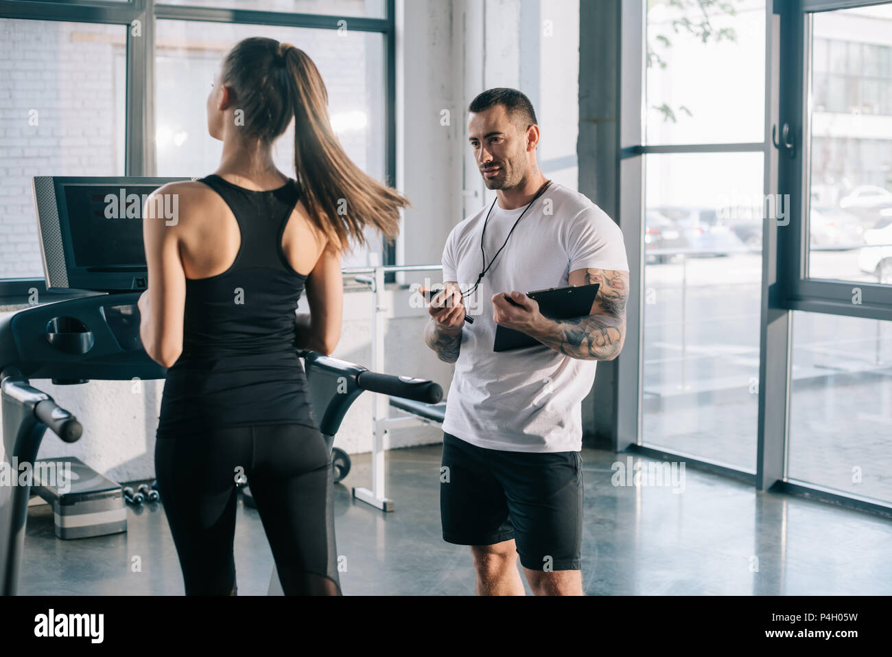 male personal trainer using timer while sportswoman running on ...