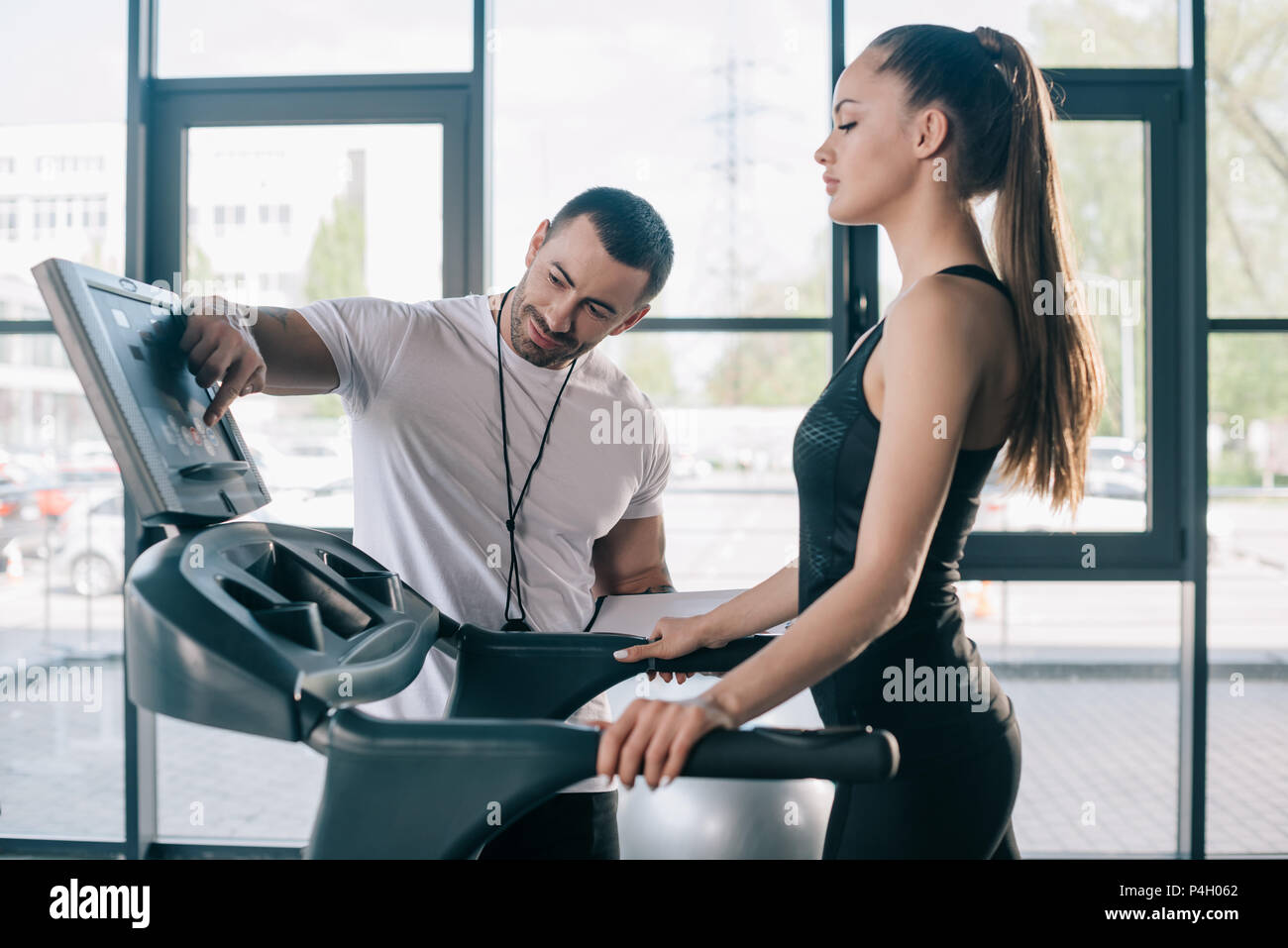 male personal trainer pointing at treadmill screen and sportswoman ...