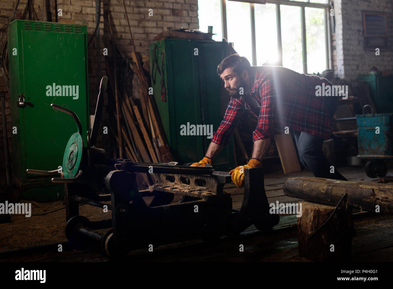 side view of worker in protective gloves pushing machine at sawmill ...