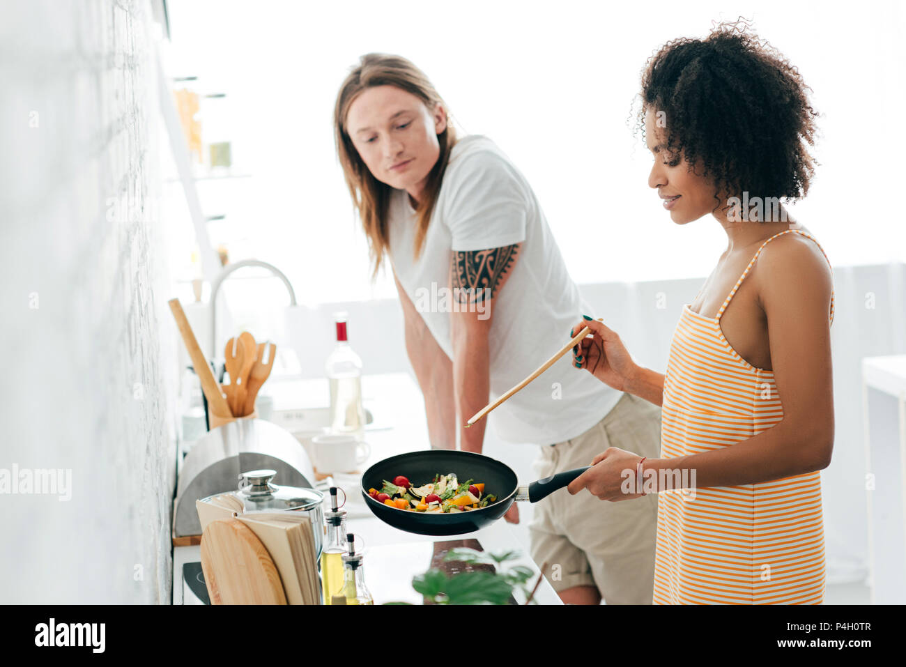 african american woman cooking vegetables in frying pan while boyfriend ...