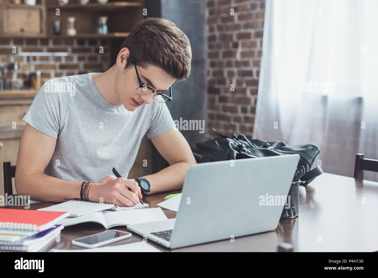 serious student writing homework at table with laptop and smartphone ...