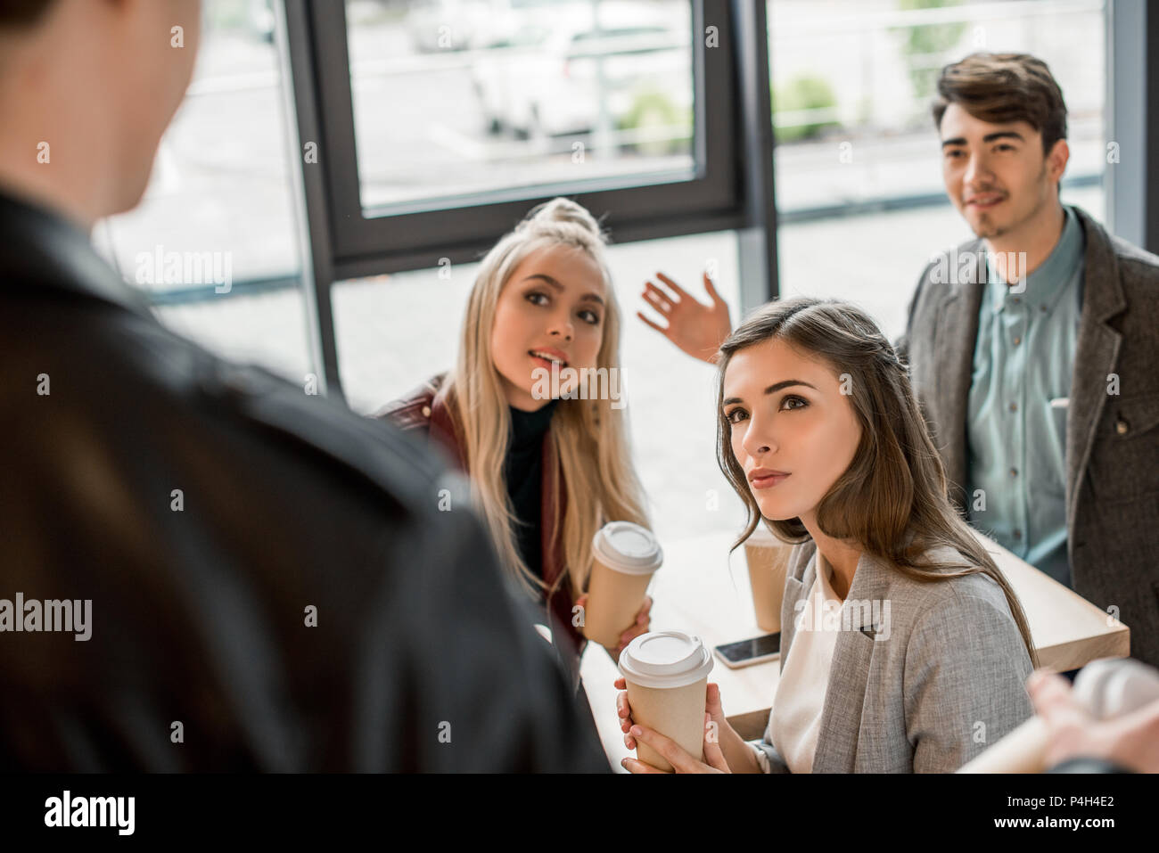 Three friends looking at friend and showing different gestures in cafe ...