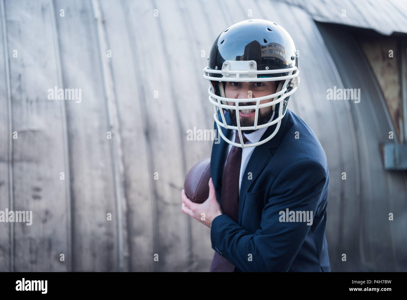 angry businessman in suit and rugby helmet with ball in hands on street ...