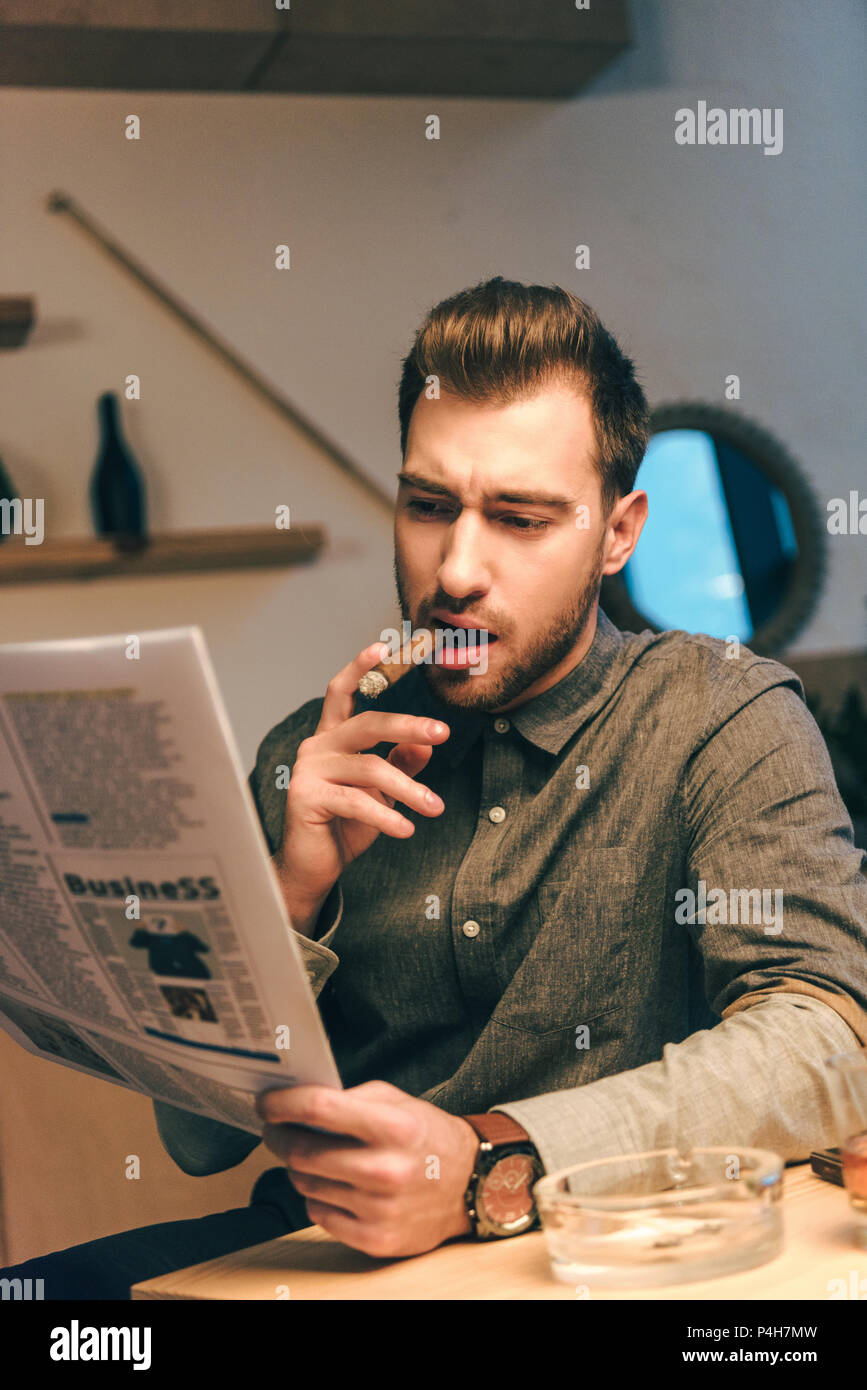 portrait of confident businessman smoking cigar while reading newspaper ...