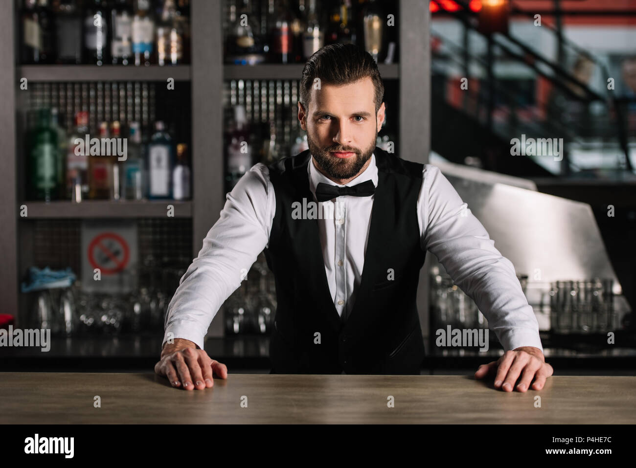 handsome bartender leaning on bar counter and looking at camera Stock ...