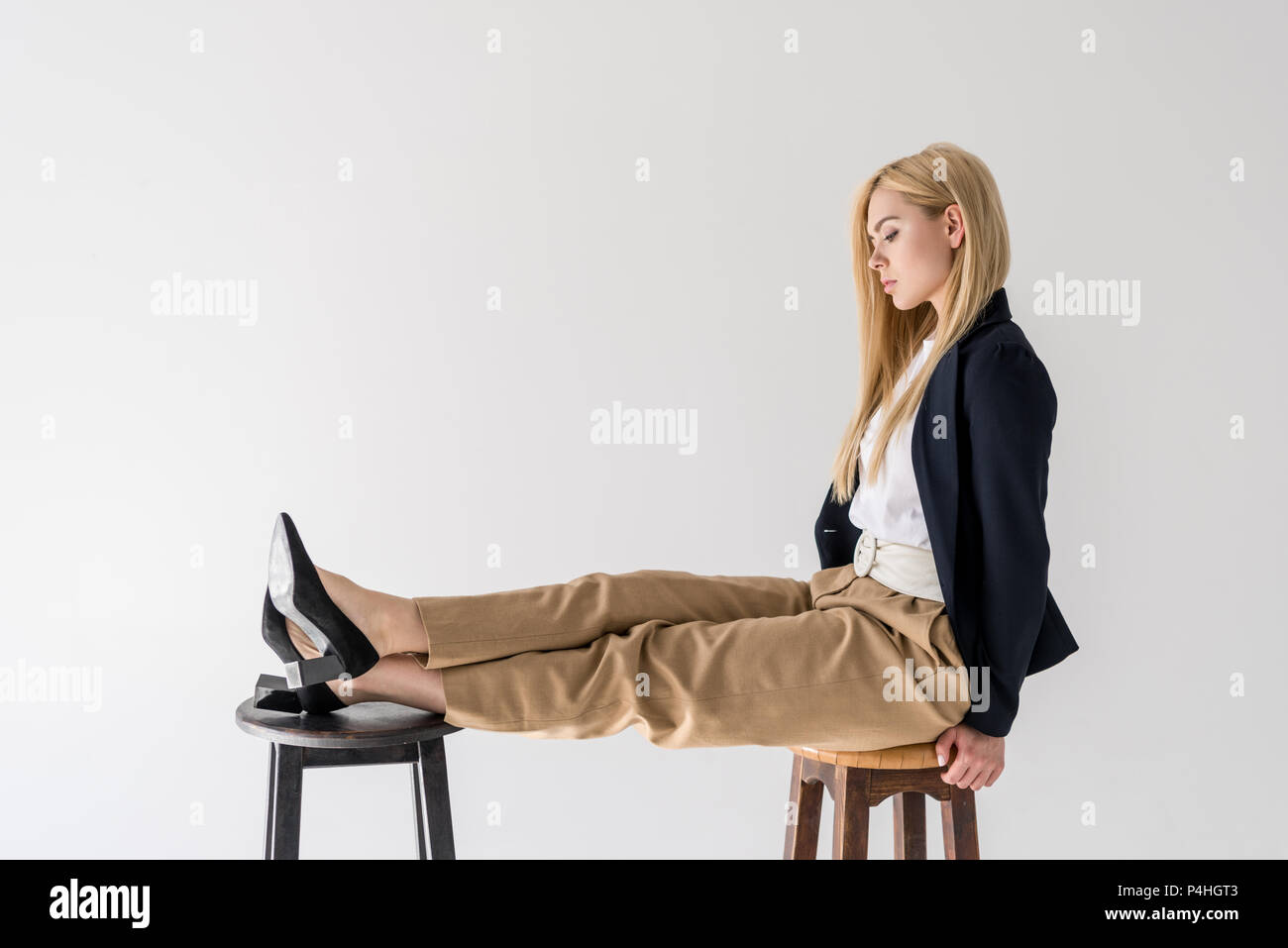 side view of beautiful fashionable blonde girl sitting on stool and ...