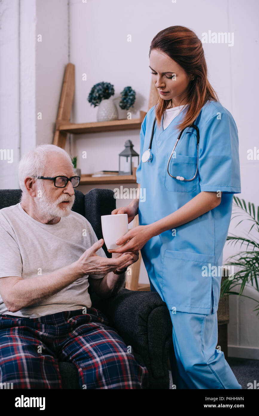 Nurse giving cup with drink to senior patient Stock Photo - Alamy