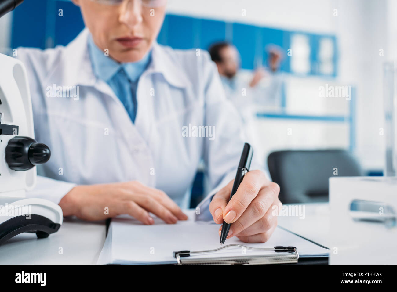 partial view of female scientist making notes in notepad at workplace ...