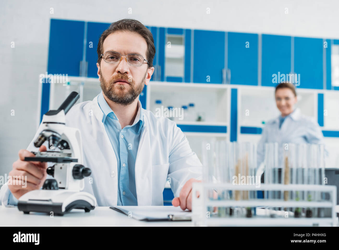 selective focus of scientist in white coat and eyeglasses at workplace ...