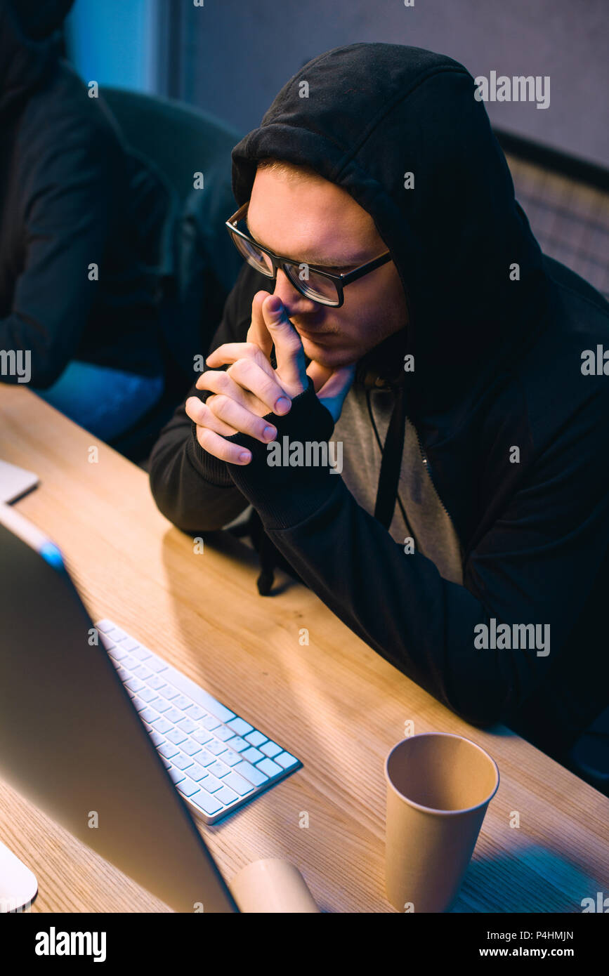 thoughtful hooded hacker looking at computer screen Stock Photo - Alamy