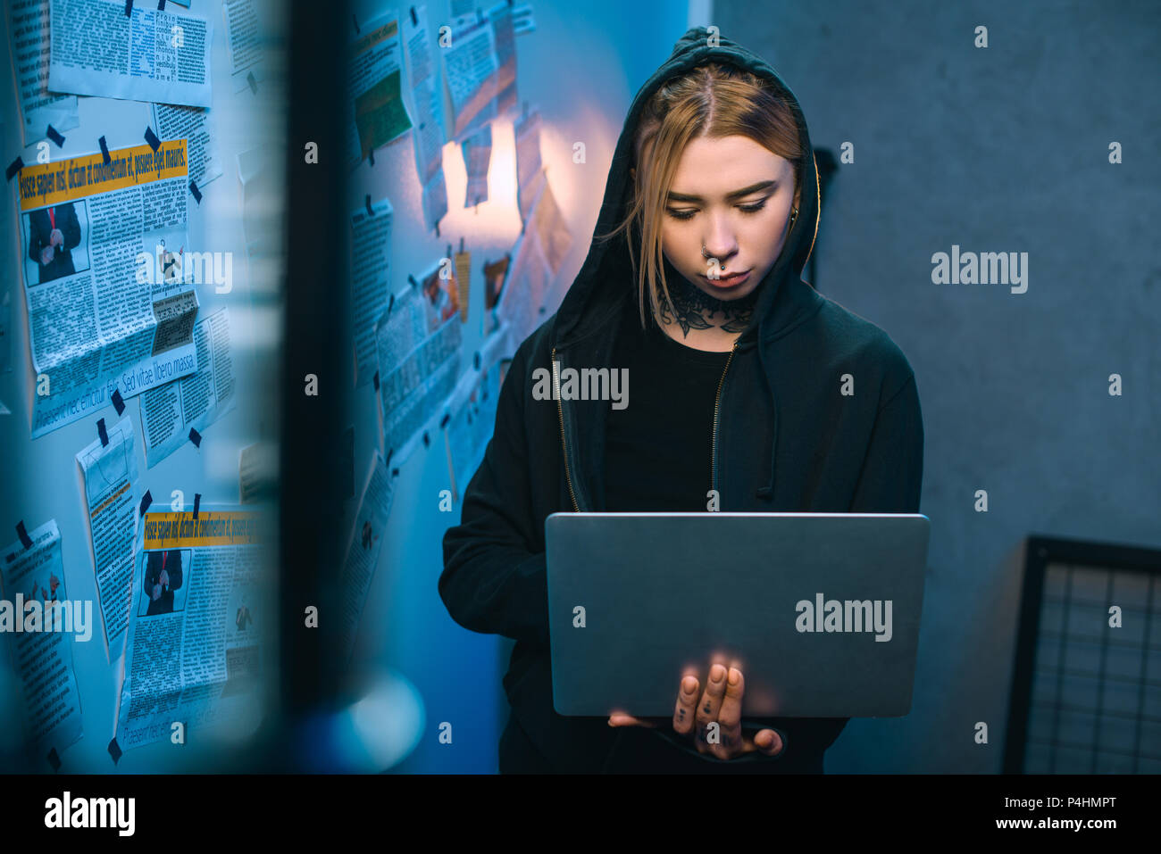 young female hacker with laptop standing in front of wall with ...