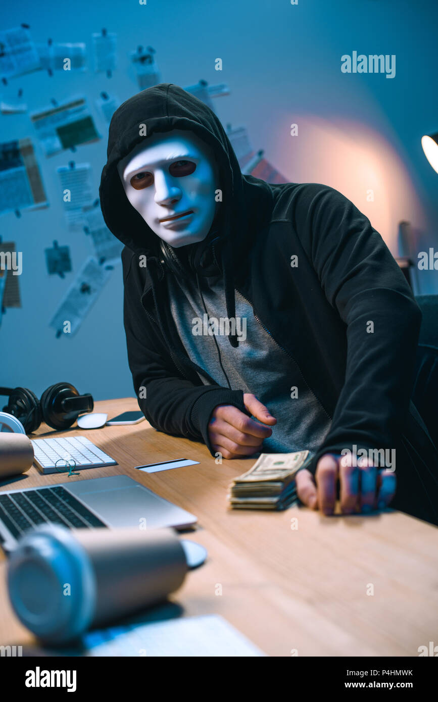 hacker in mask with stack of money on desk Stock Photo - Alamy