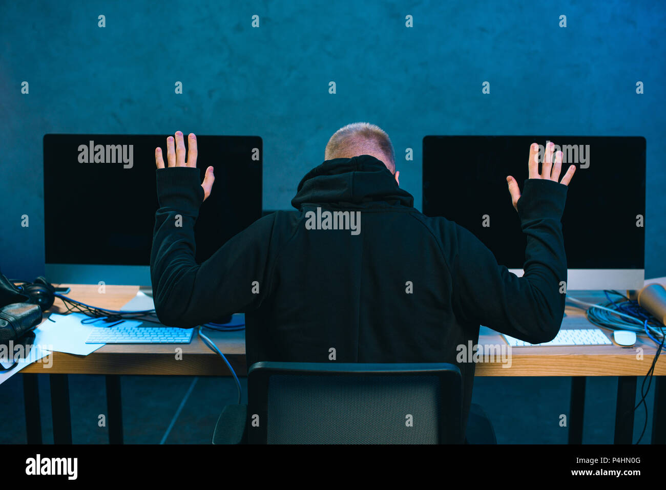 rear view of arrested hacker with raised hands in front of workplace ...