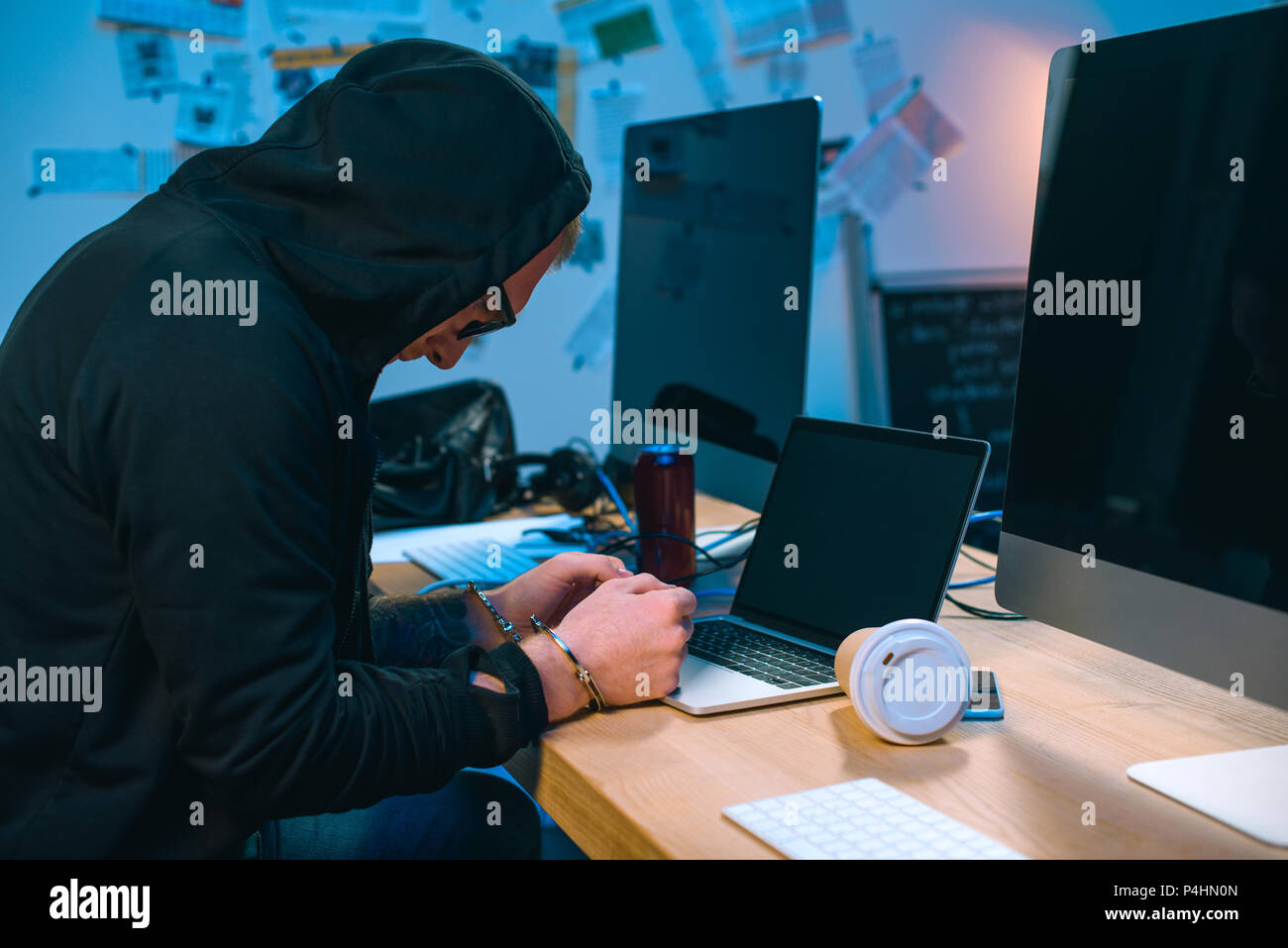 handcuffed hacker in hoodie in front of laptop at workplace Stock Photo ...