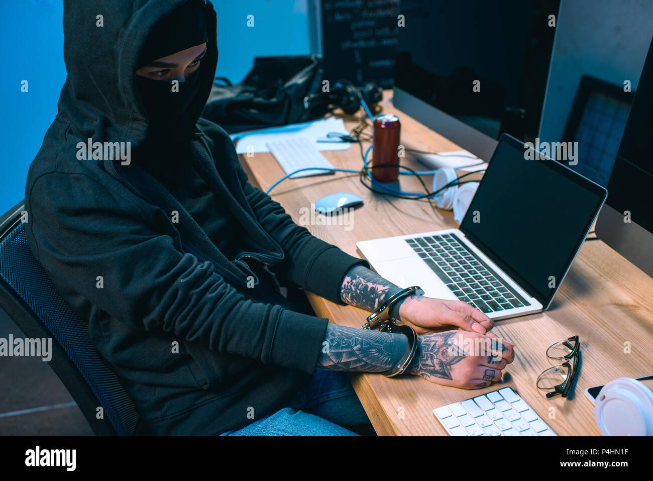 busted hacker in mask with handcuffs in front of workplace Stock Photo ...