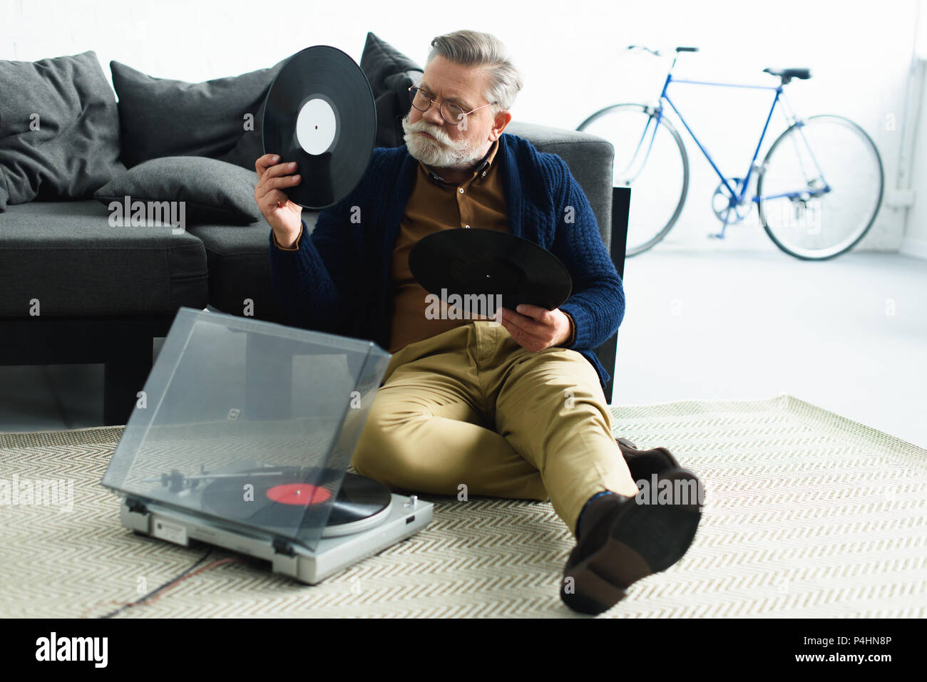 stylish senior man holding vinyl records while sitting on carpet at ...