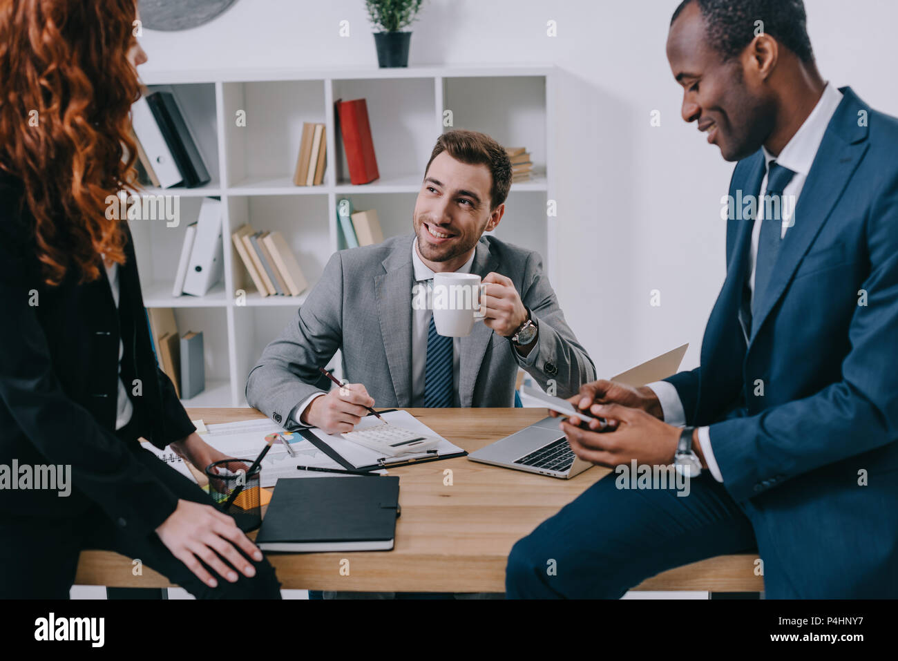 Smiling estate agent with cup of coffee talking to clients Stock Photo ...