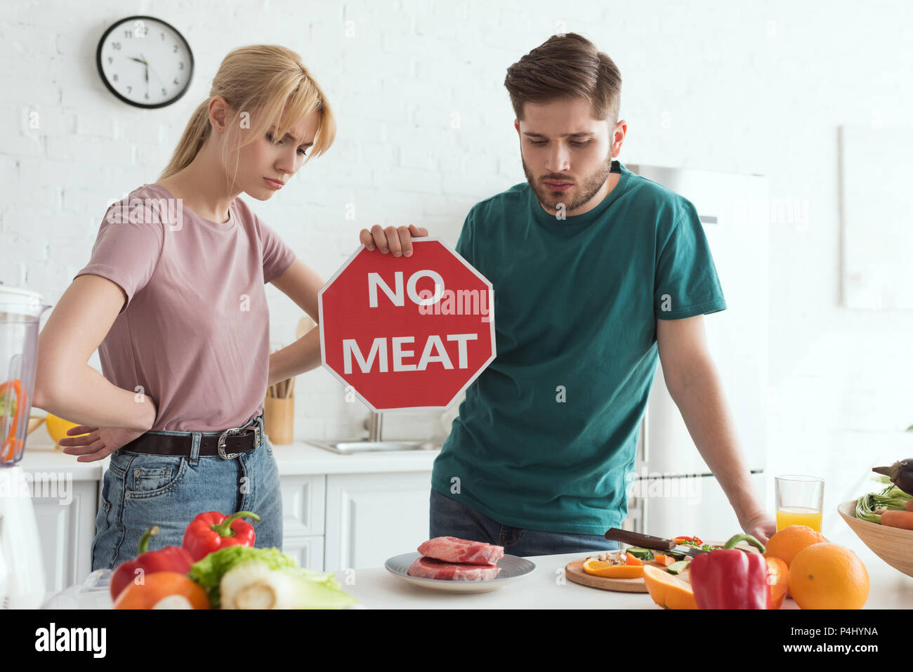 vegan couple with no meat sign at table with raw meat and vegetables in ...