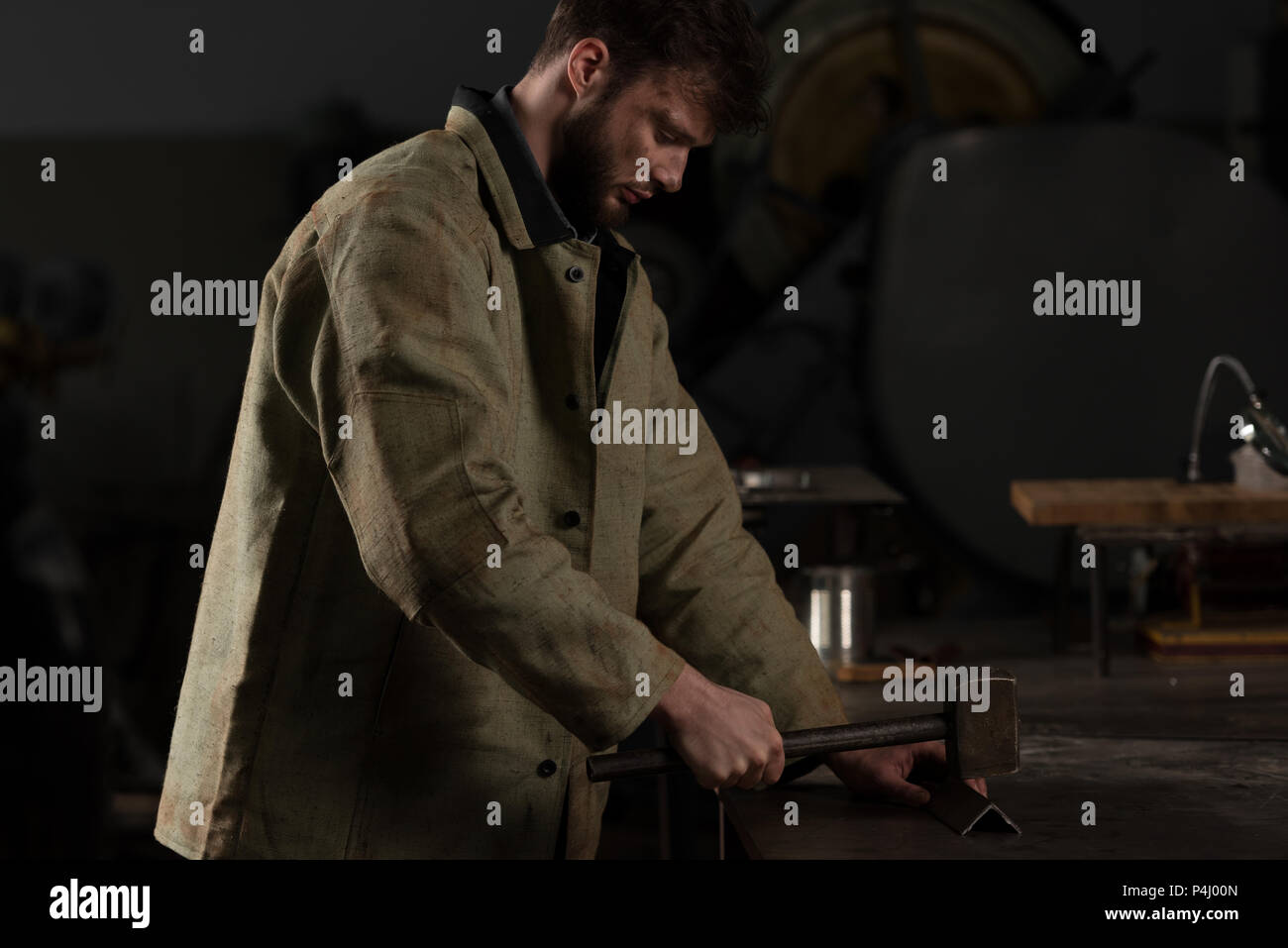 side view of young workman with hammer and metal part at factory Stock ...