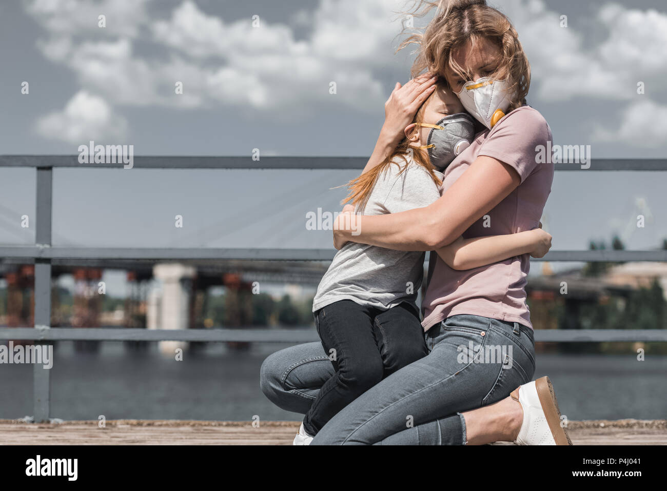 mother and daughter in protective masks hugging on bridge, air ...