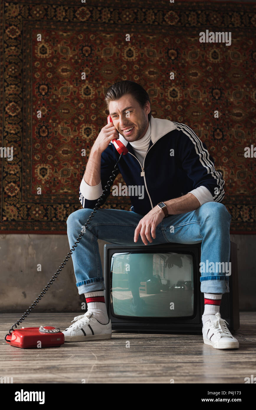 smiling young man in vintage clothes sitting on retro tv set and ...
